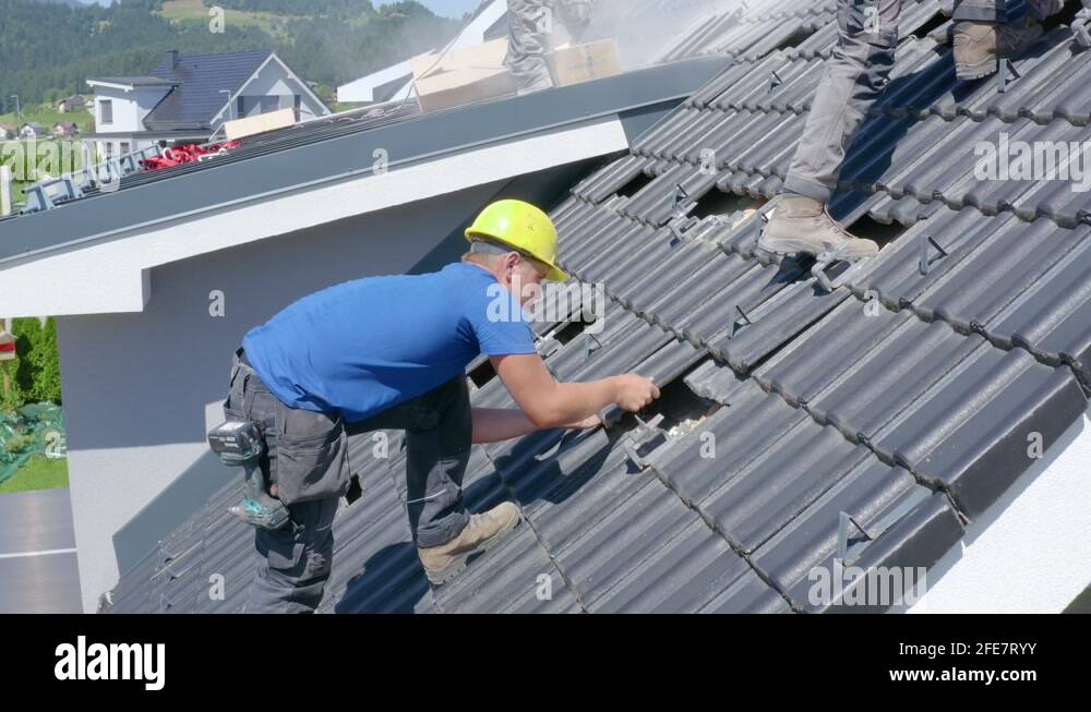 Roofer placing tiles in a house roof. Side view of construction work ...