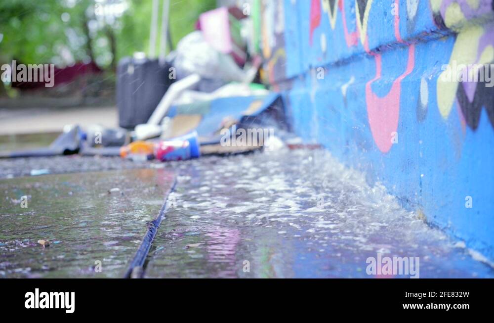 Rain pouring heavily on litter next to a graffiti wall, in an urban ...