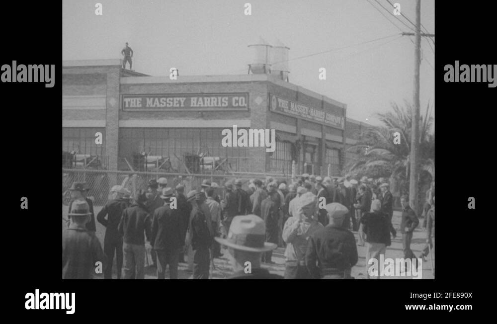 1930s California: Crowd of men gather outside factory. Man stands on ...