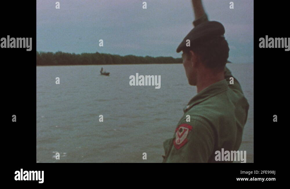 1960s Vietnam: Soldier waves to boat on river. Soldiers toss rope to ...