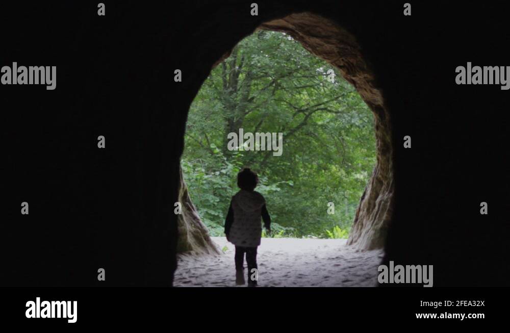 Lost child little girl walking out of a cave entrance. Helmes cave in ...