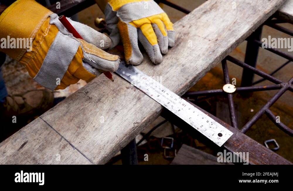 Construction worker using tape measurements to measure plank and pencil ...