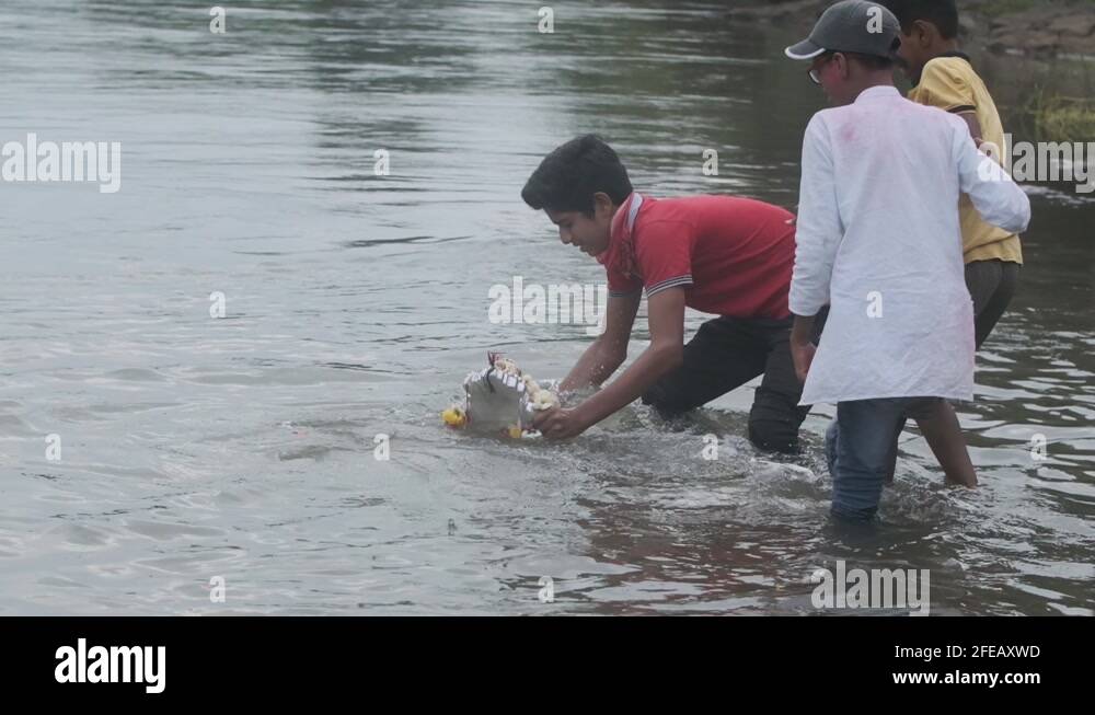 Indian children standing in a river dipping and immersing ganpati ...