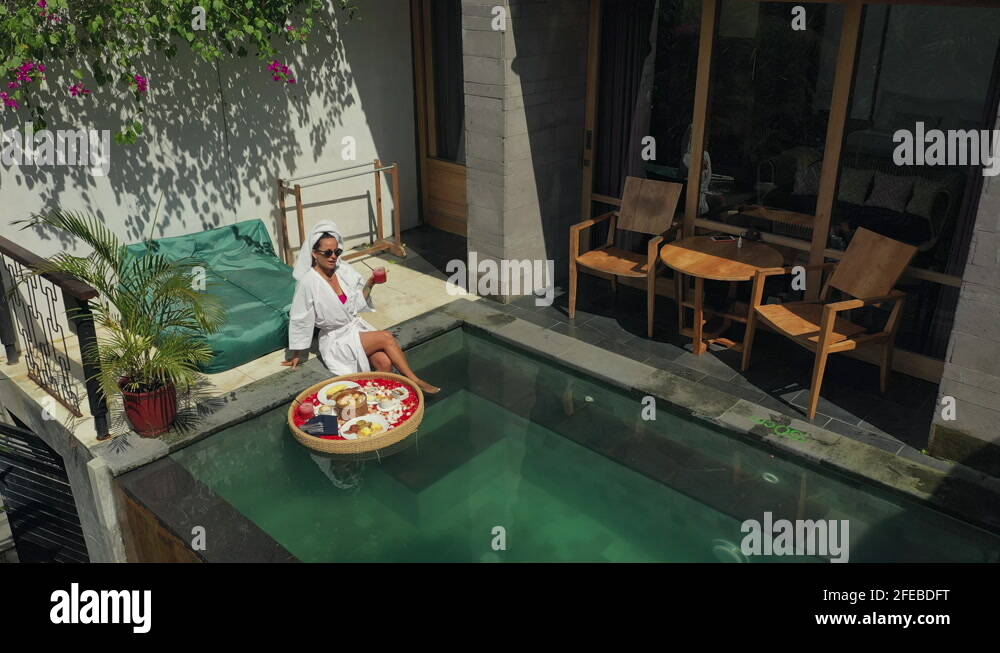 Alone female on holiday in a white robe relaxing by a pool with a ...