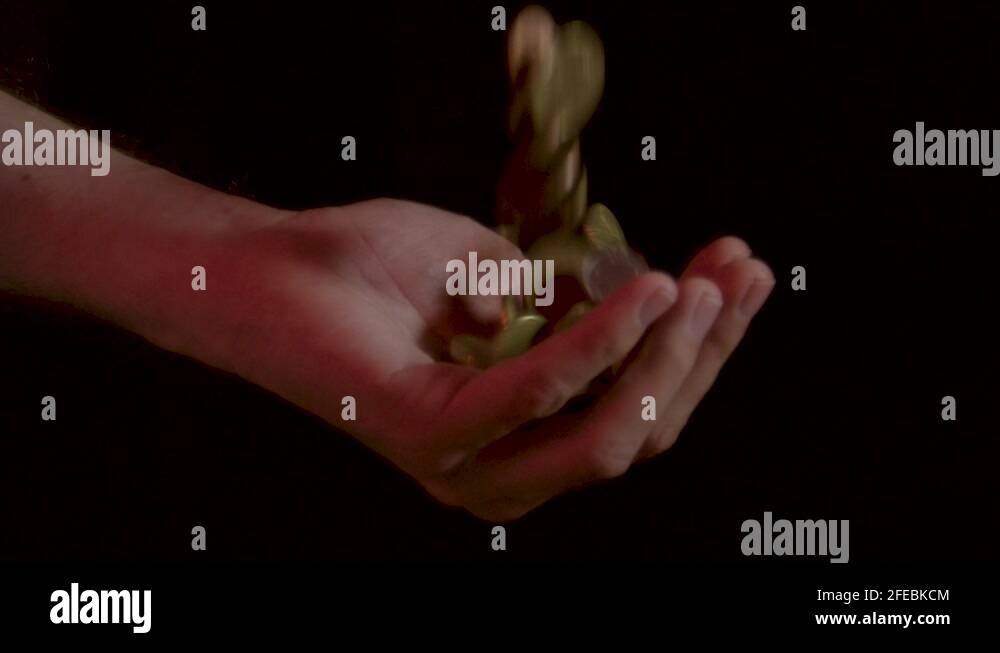 Coins money falling into a hand red lighting and a black background in ...