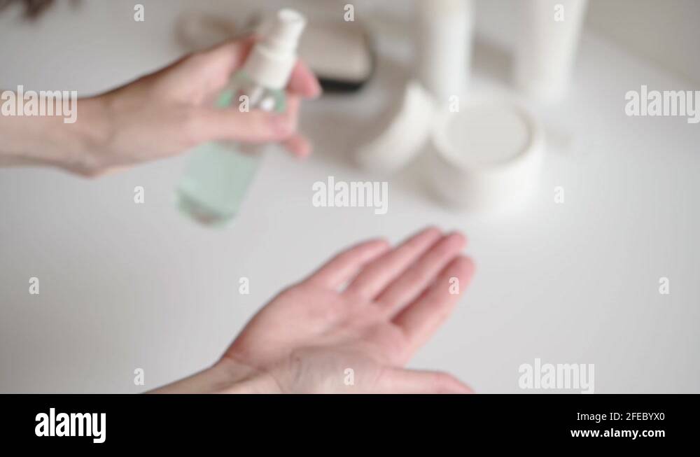 Woman at the table with cosmetics splash antiseptic lotion on her hands ...