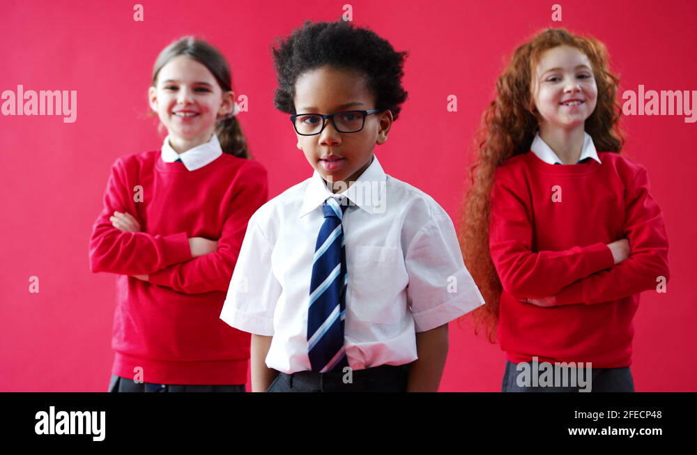 Group Of Elementary School Pupils Wearing Uniform Smiling Against Red ...