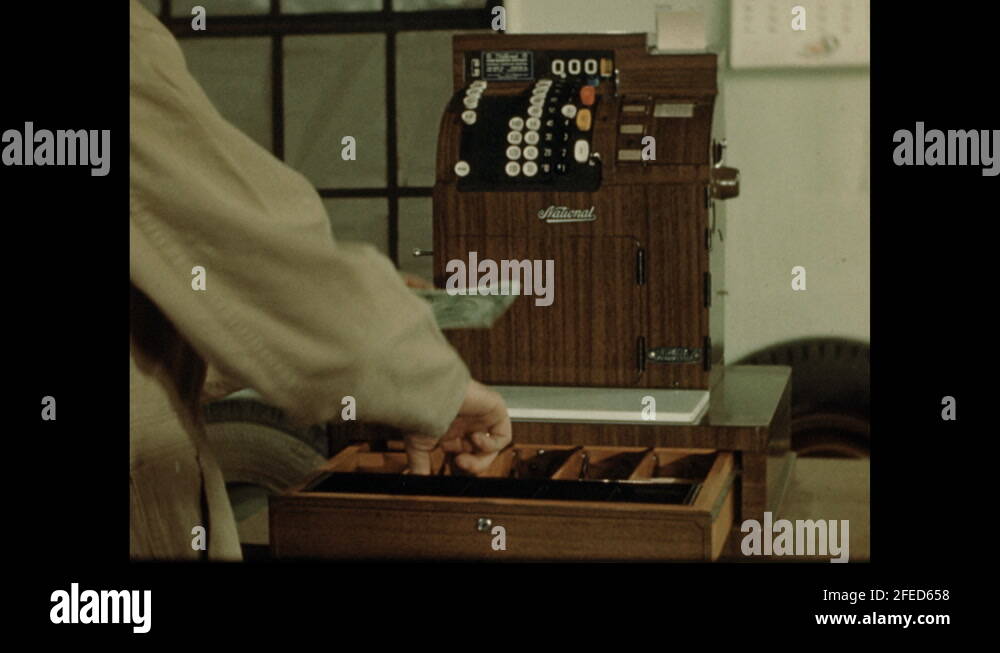 1950s: Man opens cash register and takes out bills. Numbers 587 for ...