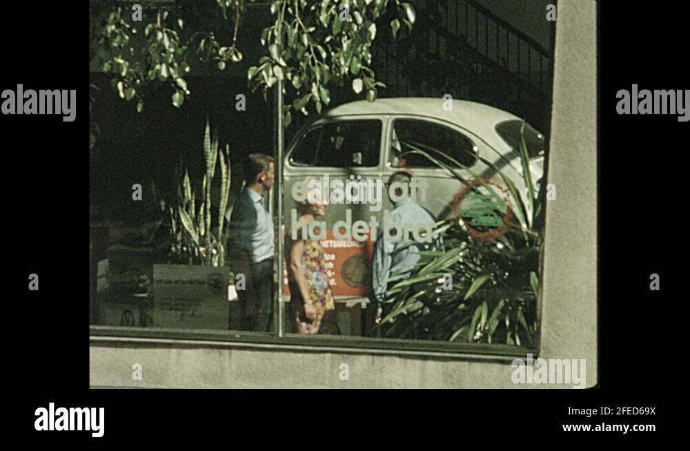 1970s: Looking in window of car dealership where three people are ...