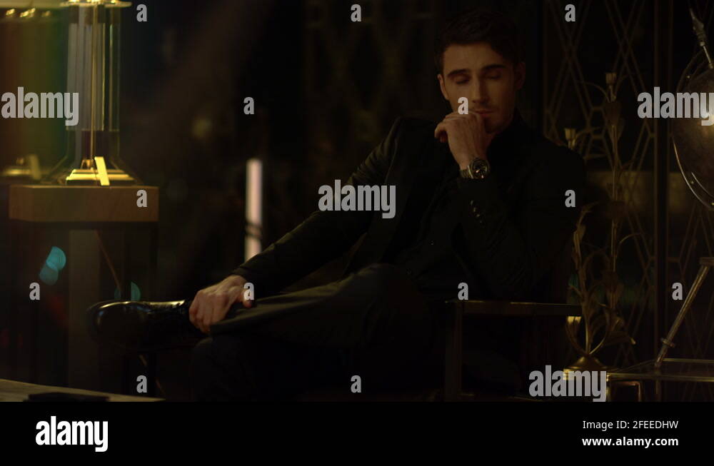 Rich man sitting crossed legs in dark room. Stylish guy contemplating ...
