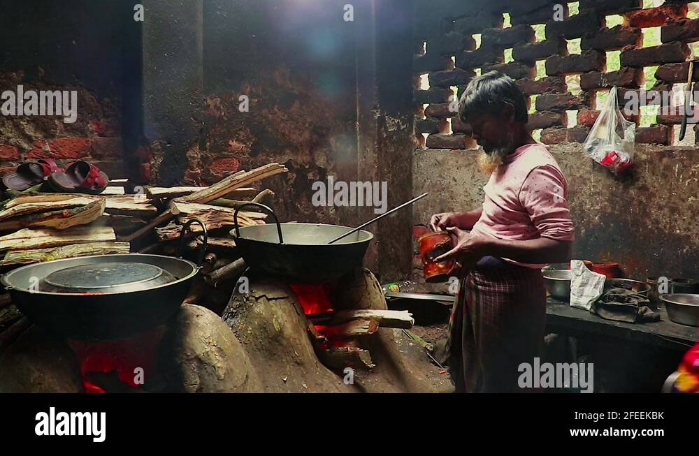 Indian Bangladesh Old Man adding spice to wok while cooking in kitchen ...