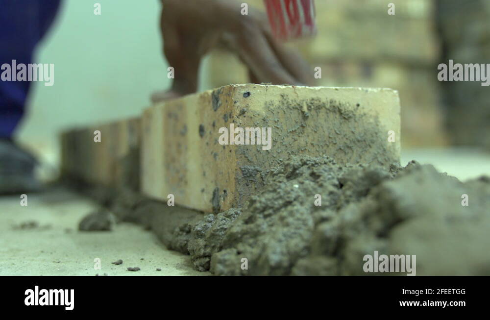 Close up. African bricklayer hand lays brick in cement and uses ...