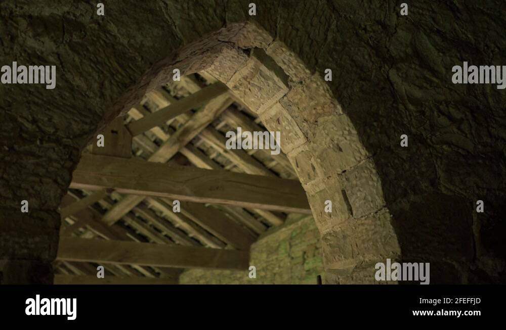 Archway entrance in old stone building with wooden roof rafters panning ...