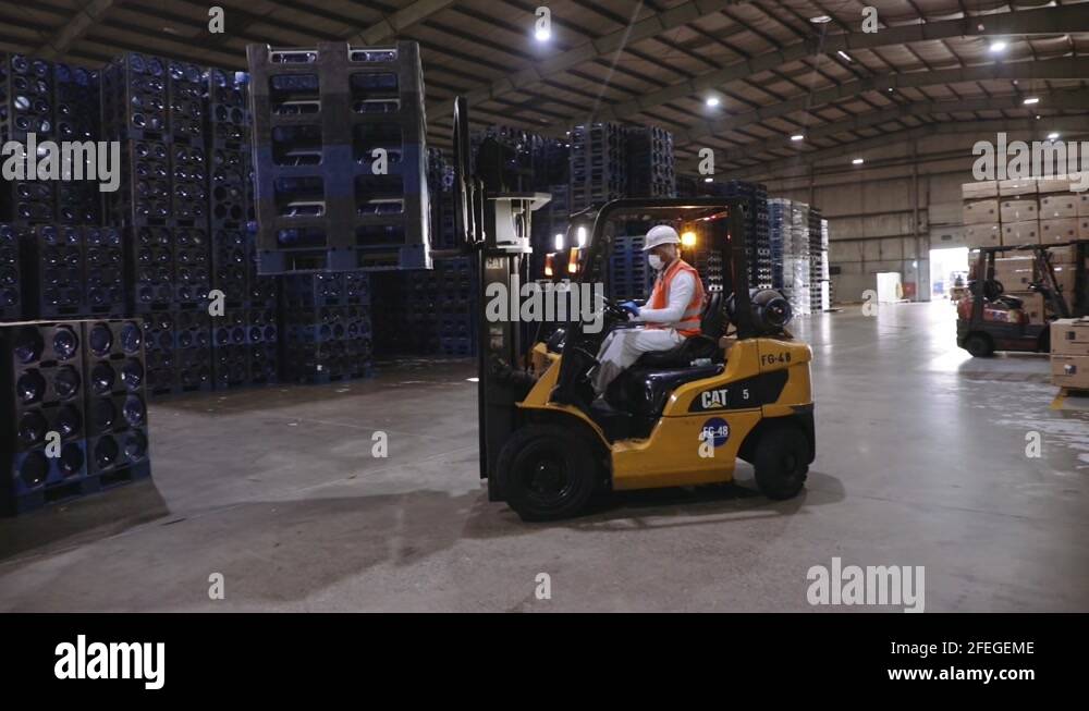 Forklift truck driver loading gallon water bottle stack onto industrial ...