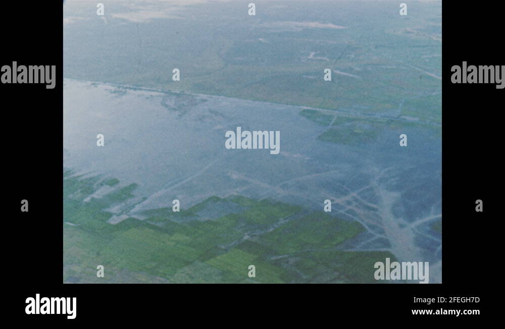 1960s: Flying over field of farms, crops. Man in helicopter fires ...