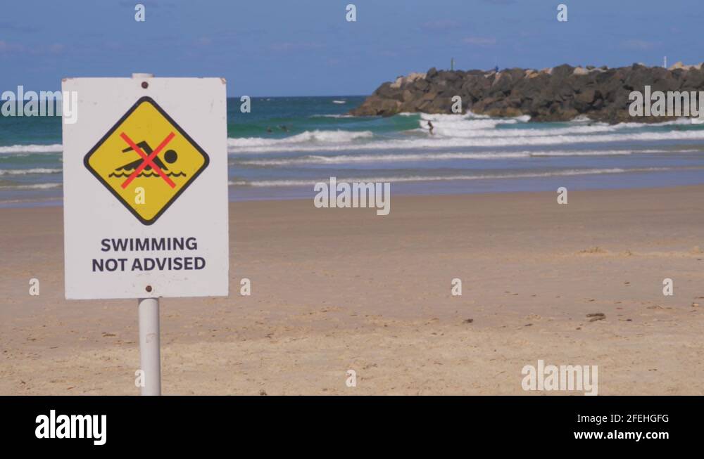 Swimming Not Advised Signage On The Beach Shore - Tourists Surfing At ...