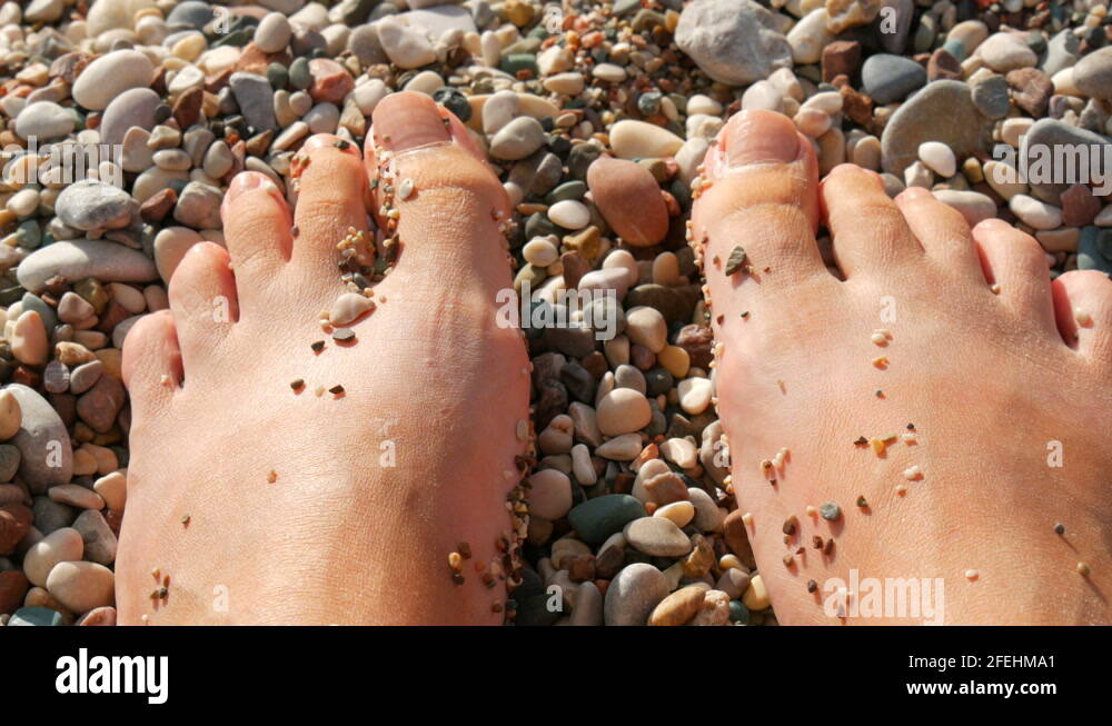 Female toes on the beach of rocky pebble sand on the seashore in summer ...