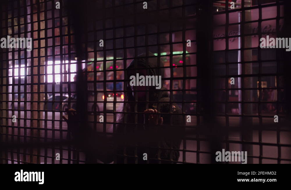 Woman wearing creepy mask and hood behind chained gate looks at camera ...