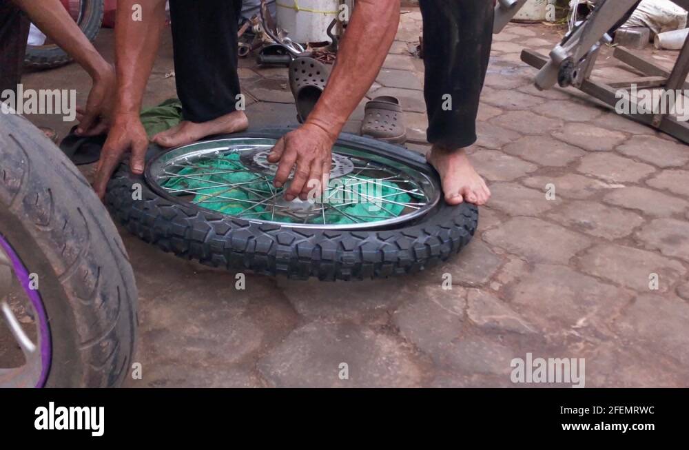 Tire lever and bare feet install new moto tire on rim, rural Cambodia ...