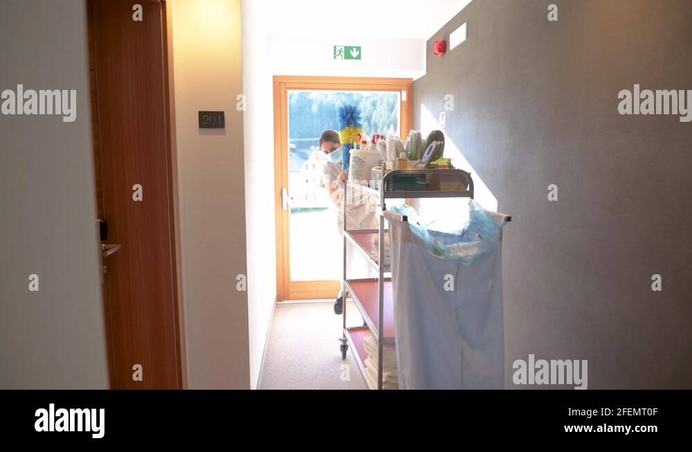 Housekeeping lady with face mask and the floor trolley walks through a ...