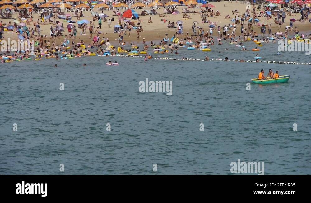 A lot of people at crowded bathing sandy beach.Boat & People swim in ...