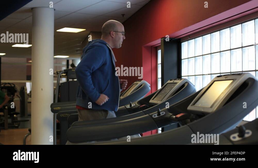 In a gym working out a bald and overweight man is running on a ...