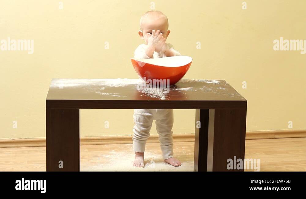Funny little child making a big mess with flour throwing down the floor ...
