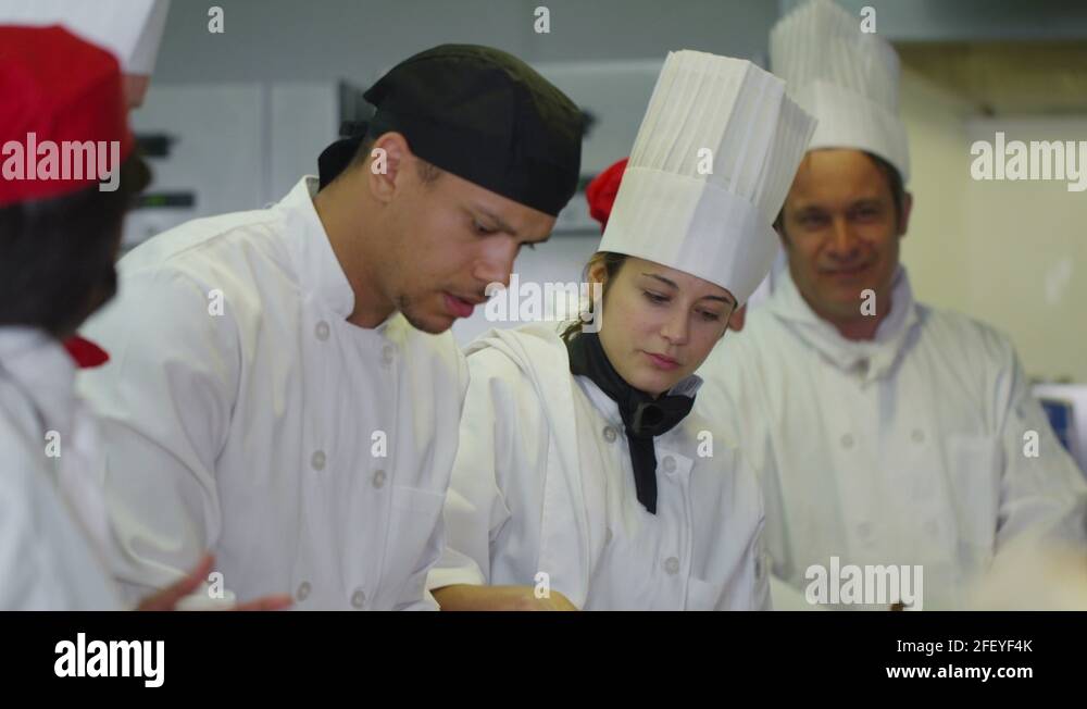 Happy team of chefs in a commercial kitchen, head chef tastes and gives ...