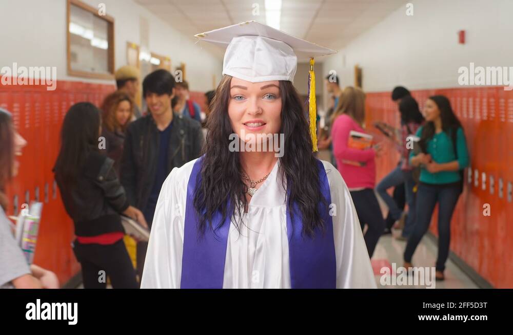 Female student wearing a graduation cap and gown stands in a hallway ...