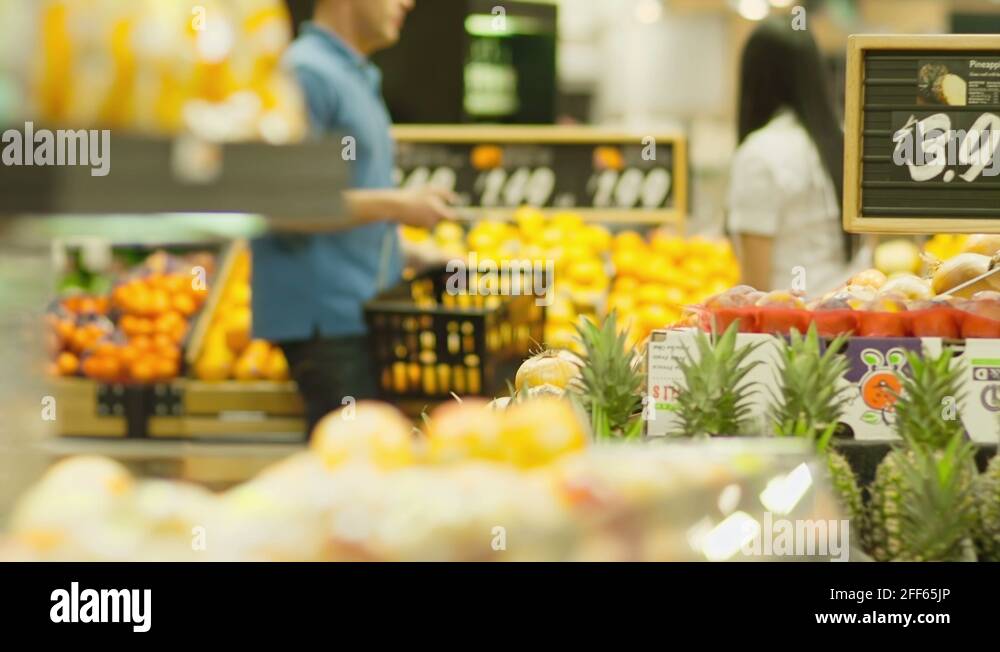 A young couple walk around a pick out produce together in a grocery ...