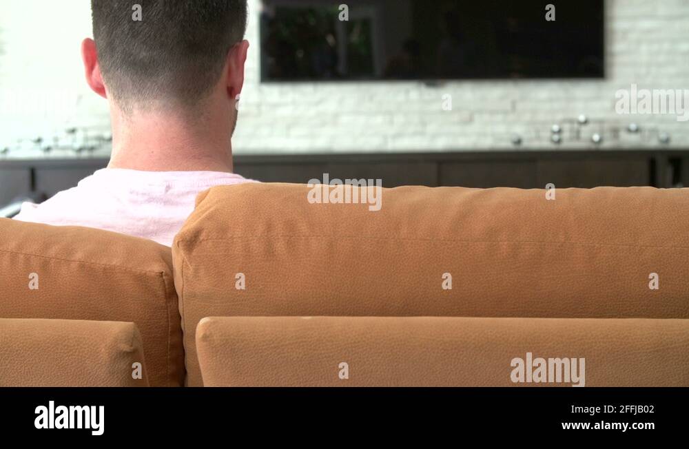 Rear View Of Man Sitting On Sofa Turning On Television Stock Video ...