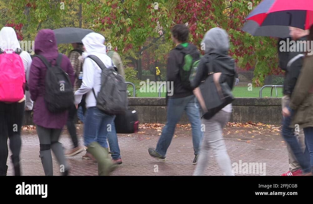 College and university students walking on campus in rain with ...