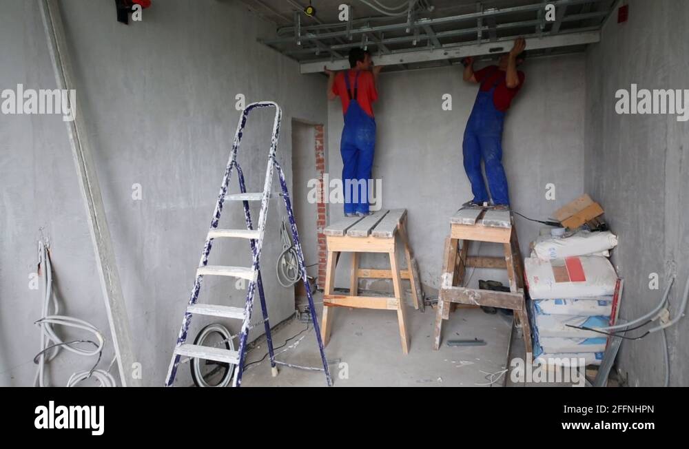 Two men in uniform install framework for hung ceiling in new flat Stock ...