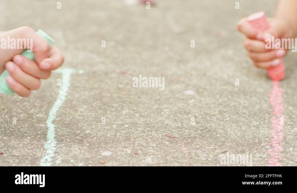 Two girls use sidewalk chalk to draw lines on the ground, in slow ...