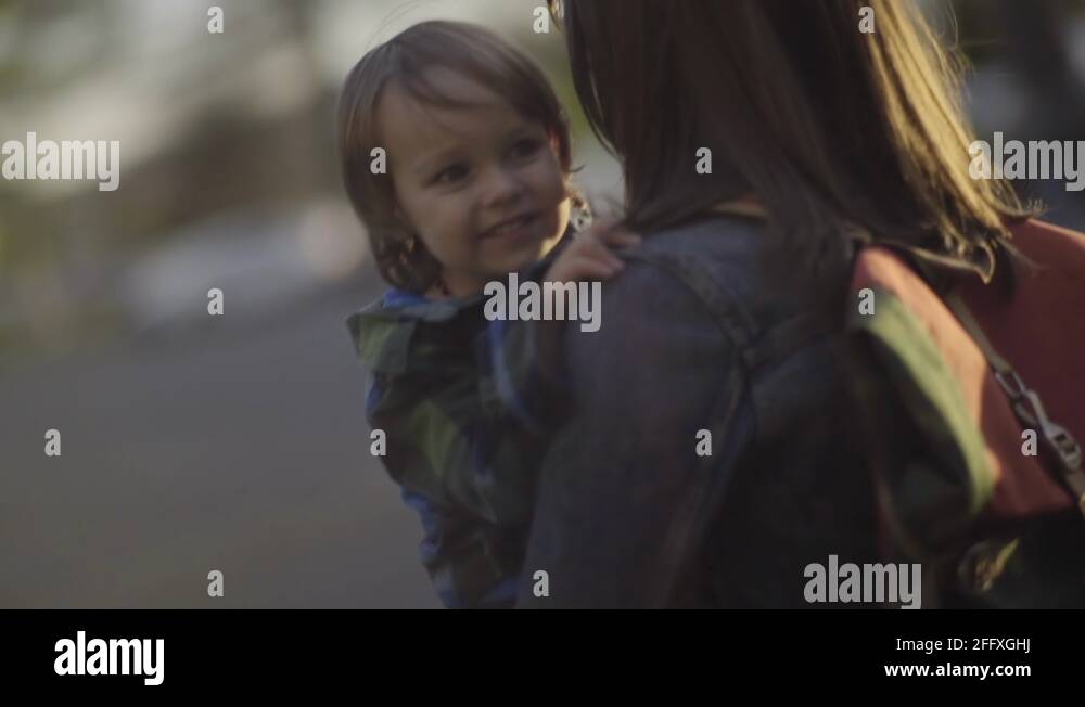 Mother Carries Her Tired Son, He Looks Over Her Shoulder, Smiles And ...