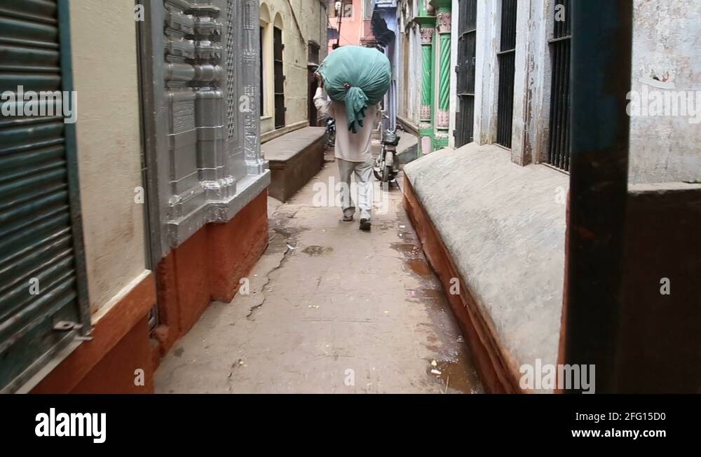 Man carrying a large sack on his back in narrow street in Varanasi ...