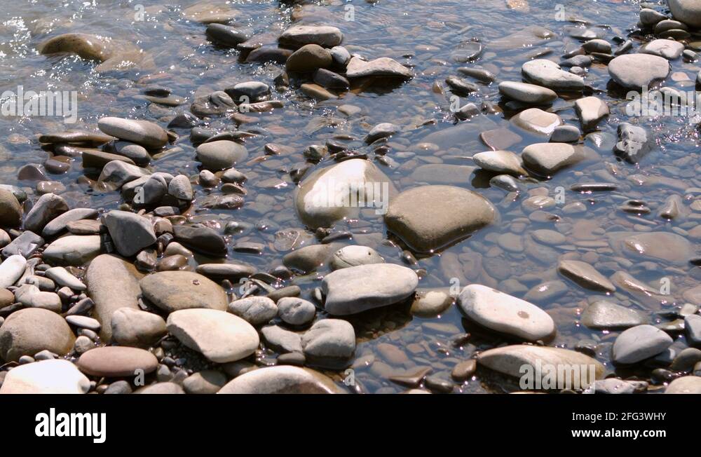 Sea pebbles in water. Ripples on the surface of water and solar patches ...