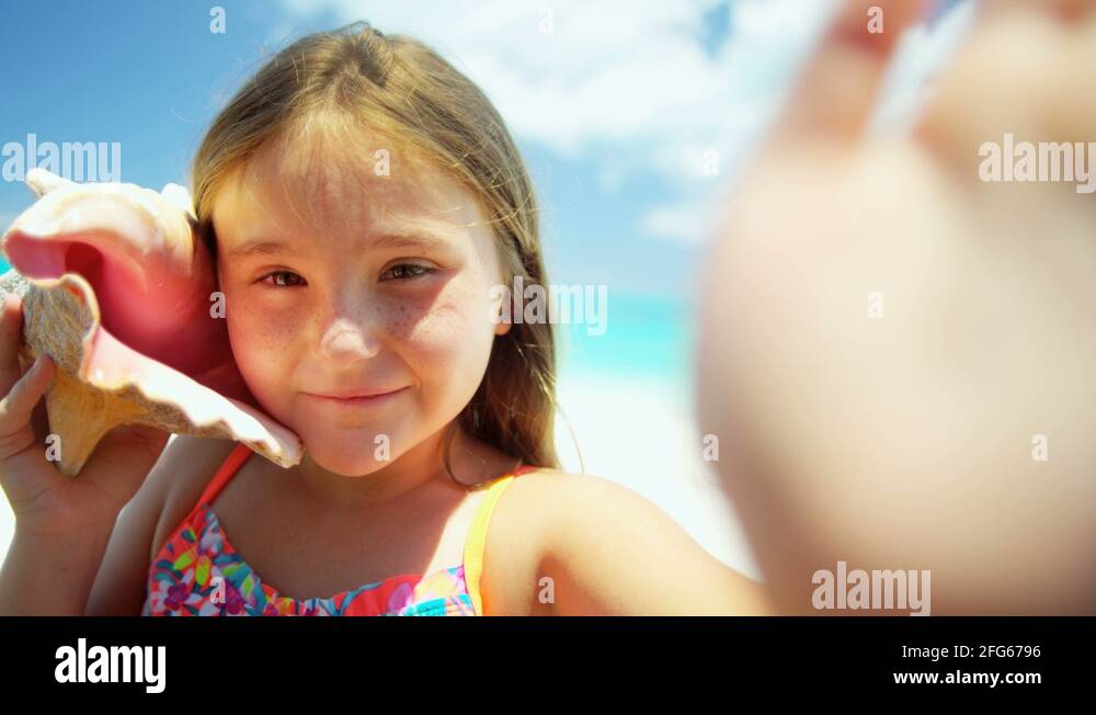 Portrait of cute smiling Caucasian girl on tropical beach holding conch ...
