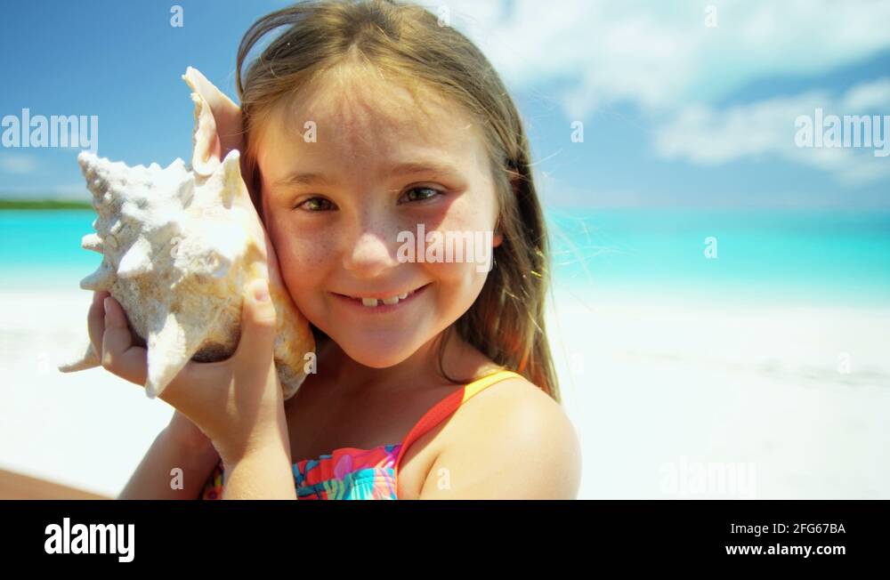 Portrait of cute smiling Caucasian girl on tropical beach holding conch ...