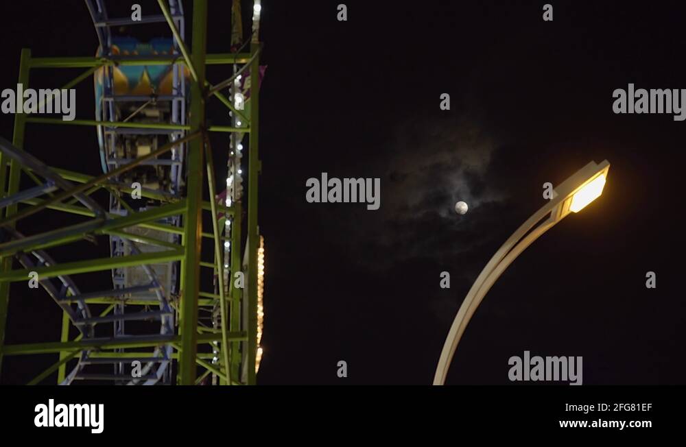 Full moon behind clouds at Amusement park as roller coaster passes by ...