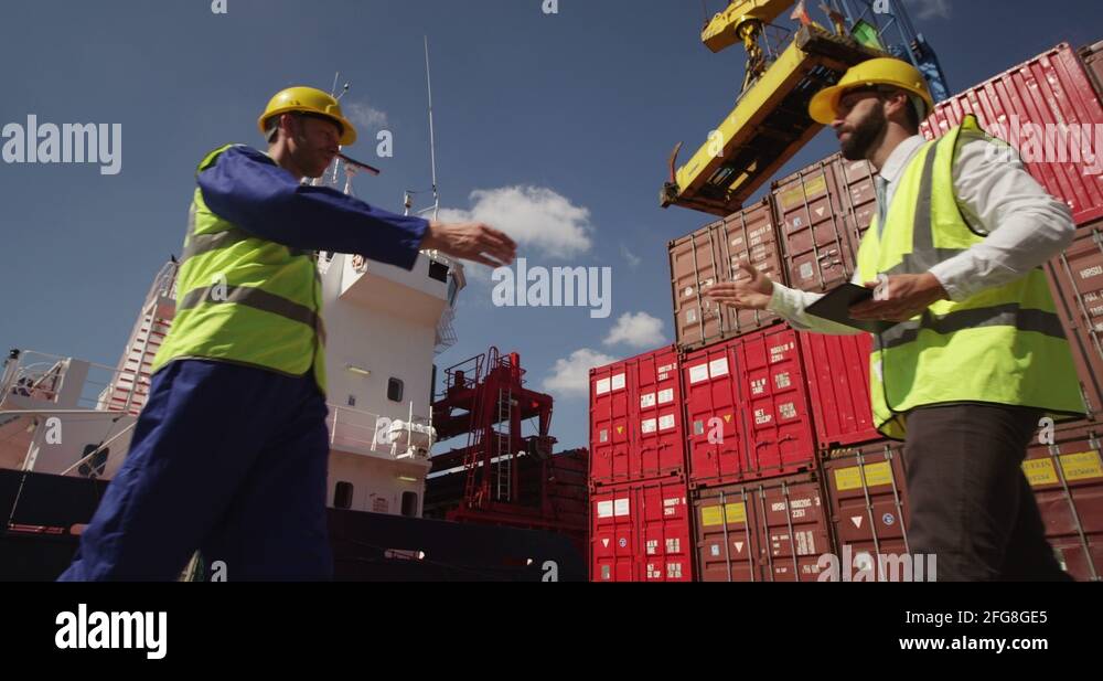 Dock workers shake hands and discuss shipping logistics in a shipyard ...