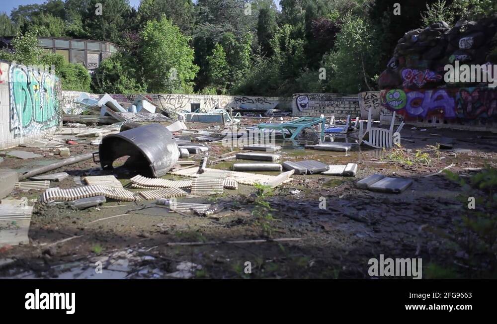 Trash, garbage and chairs in an empty abandoned outdoor pool, graffiti ...