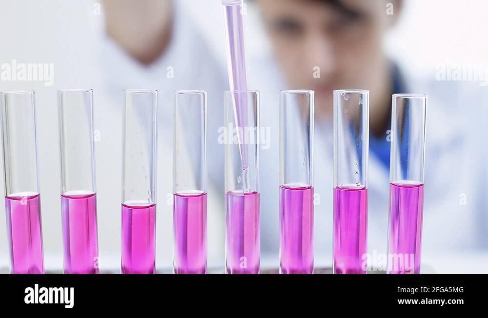 Female lab technician safety glasses pour pink liquid pipette tube rack ...