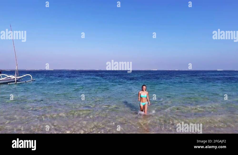 Beautiful young woman in blue bikini walking on the beach in Indonesia ...