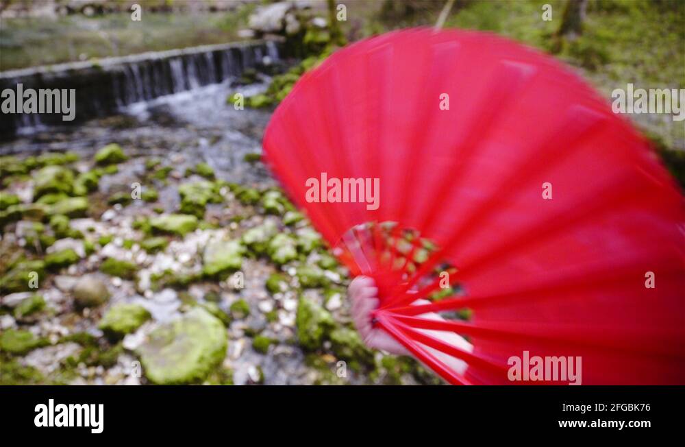Opening and closing red Chinese fan in front of natural water source 4K ...