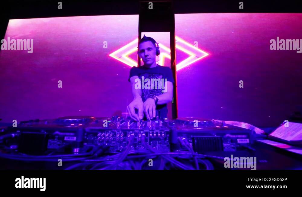 DJ is standing next to his turntable and screen on stage in club Stock ...