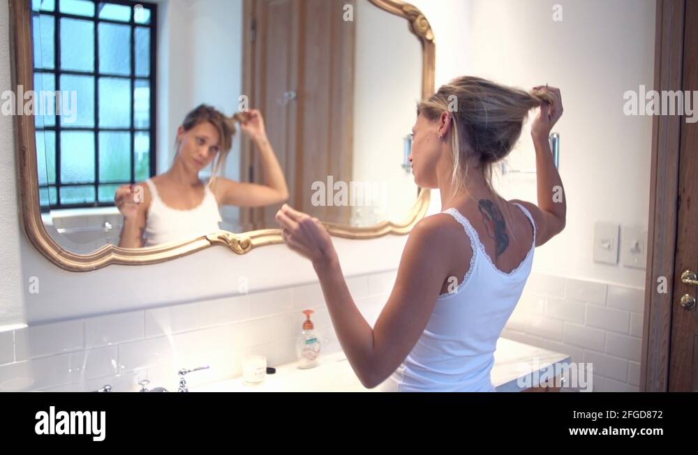 Woman fixing her hair in the bathroom mirror Stock Video Footage - Alamy