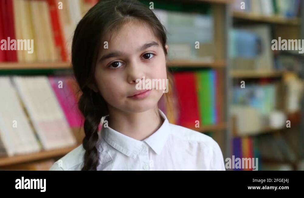 Girl with pigtail and a white blouse in the library at the book shelves ...