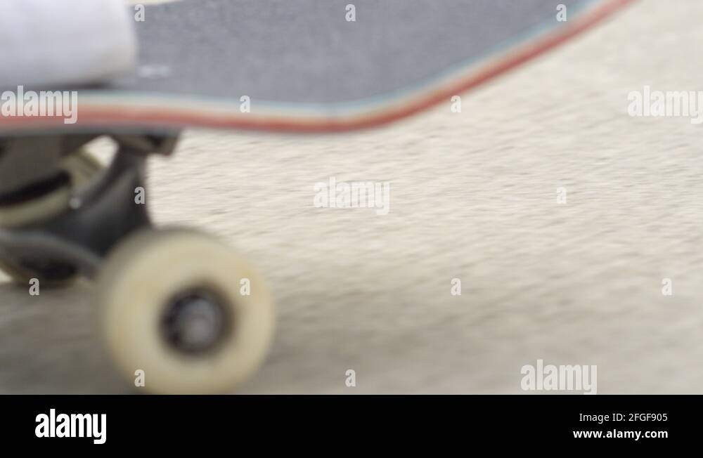 CLOSE UP: Skateboard deck and wheels spinning along the concrete street ...