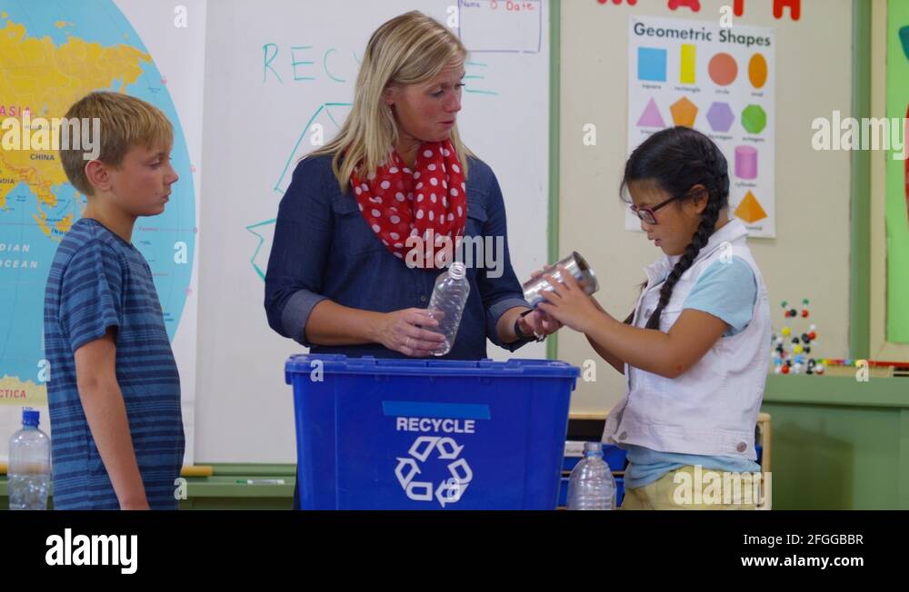 Teacher and students in school classroom putting bottles in recycle bin ...